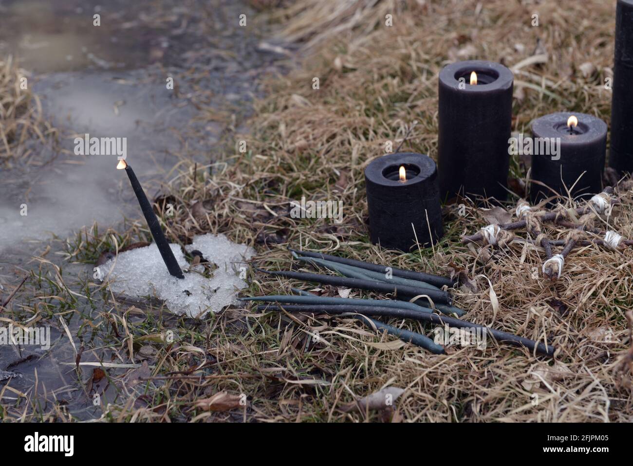 Wiccan ritual with group of black candles in grass and snow in early ...