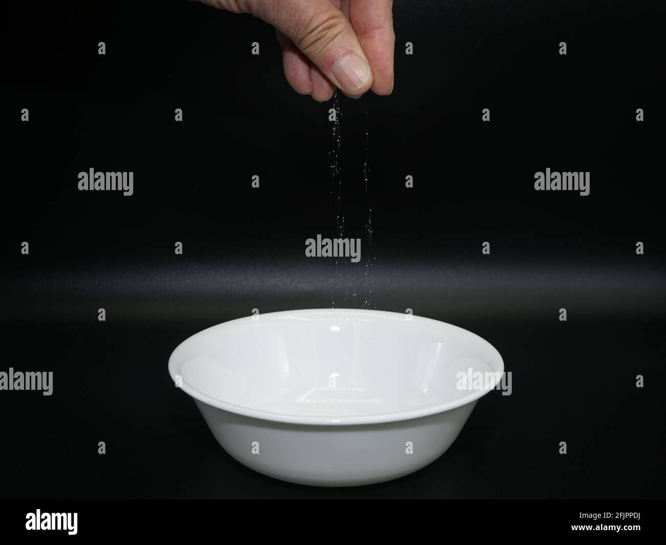 Hand sprinkling salt into bowl against black background Stock Photo - Alamy