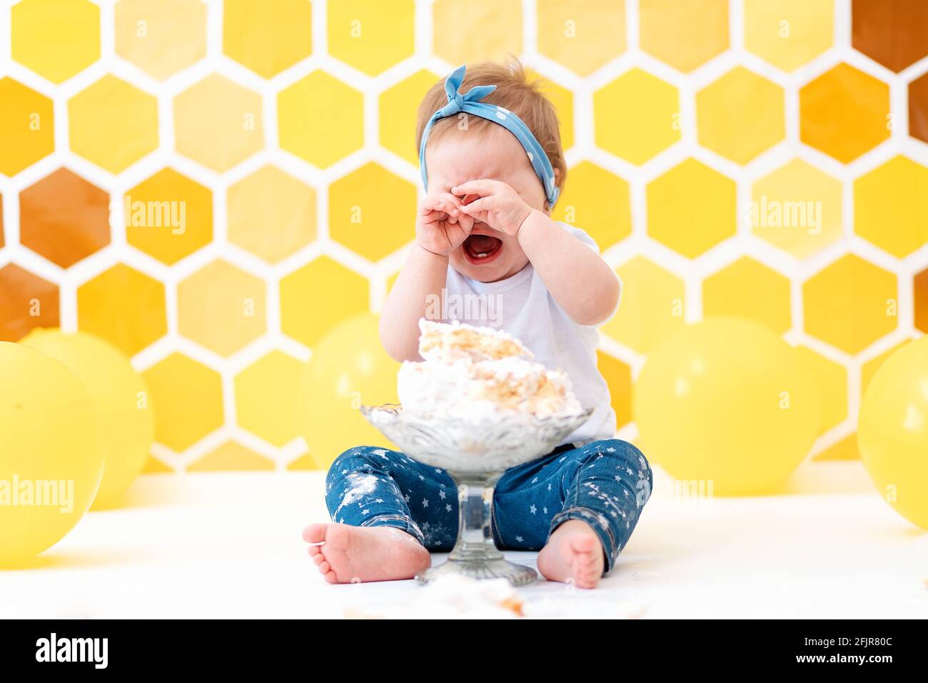 Birthday. A crying dirty toddler girl is sitting next to a broken cake ...