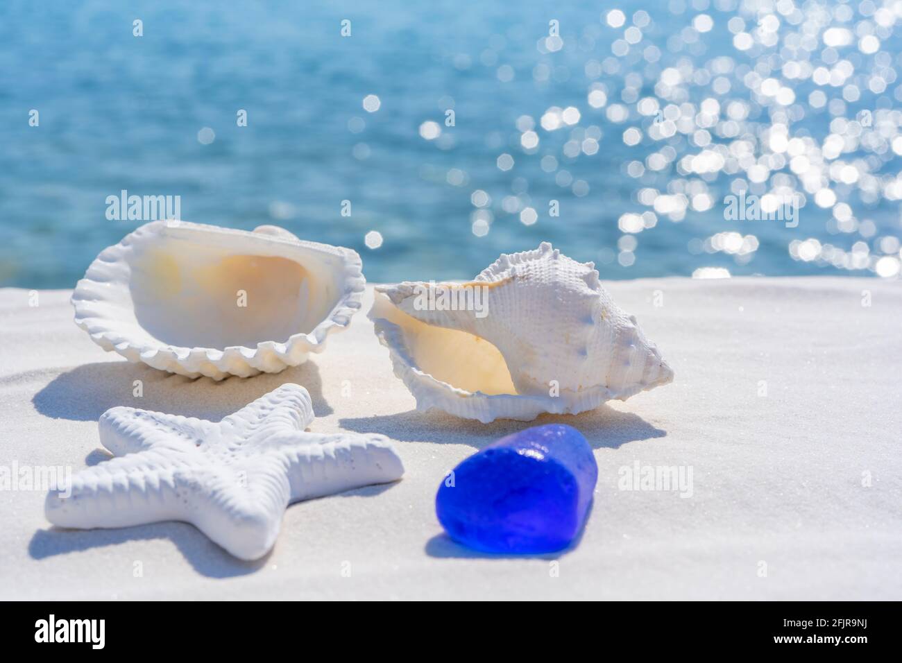 Sea shells, starfish and blue stone on a white sand and blue water ...