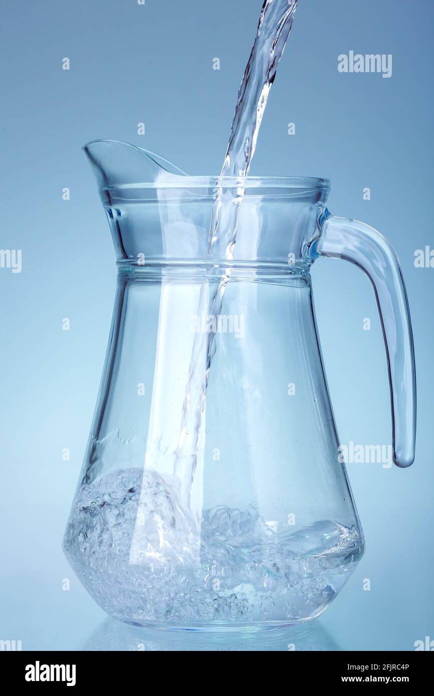 glass transparent jug is filled with a stream of water splashes at the ...