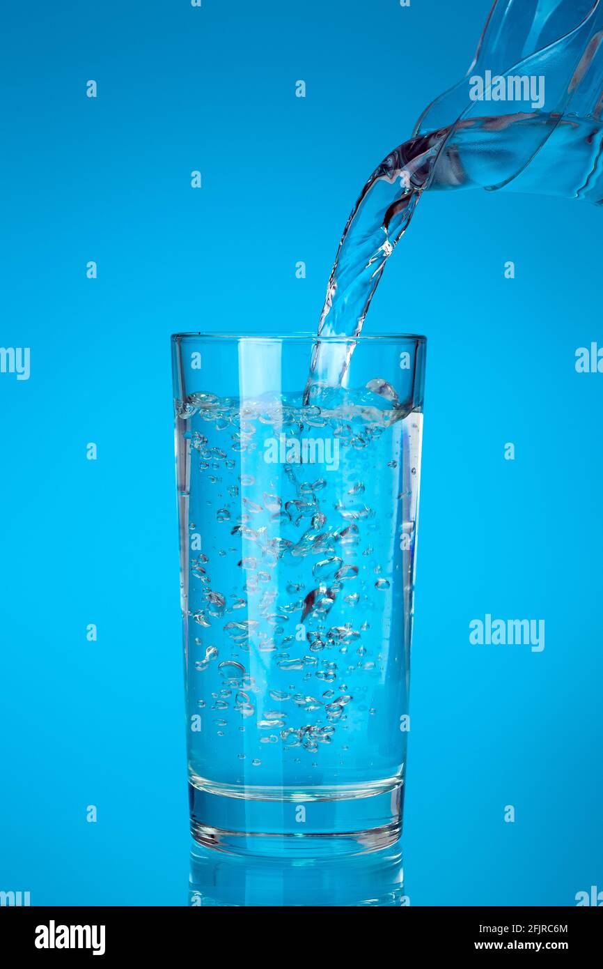 glass cup filled with a stream of fresh drinking water from a jug spout ...