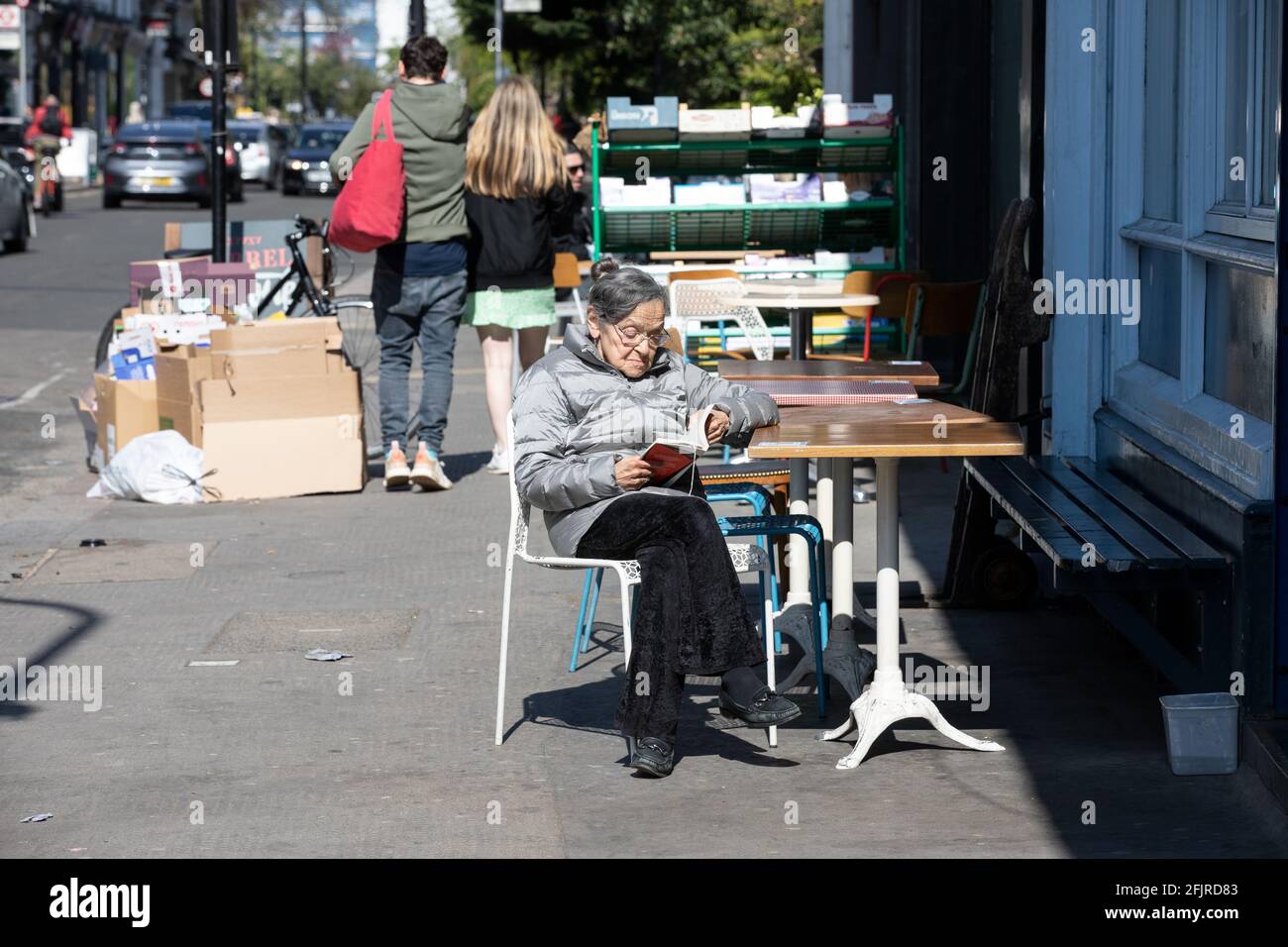 A lady sits reading a book outside a cafe in Belsize Park, London, UK ...