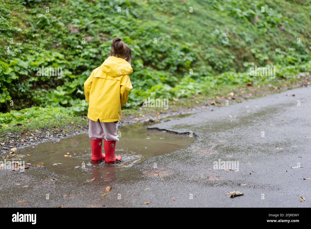 Playful girl wearing yellow raincoat while jumping in puddle during ...
