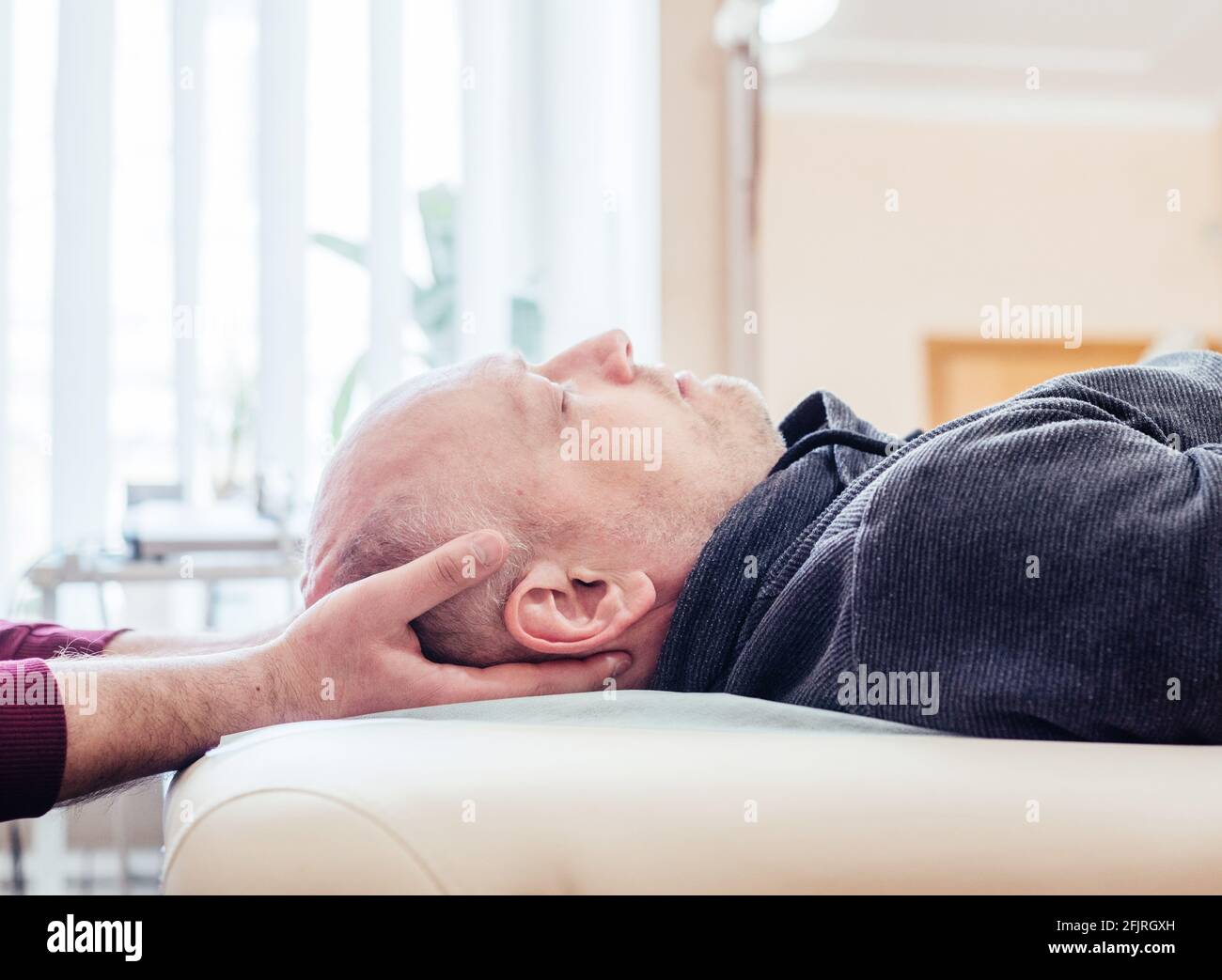 Male patient receiving cranial sacral therapy, lying on the massage ...