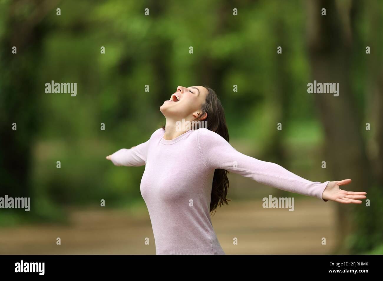 Excited woman outstretching arms and screaming in a forest celebrating ...