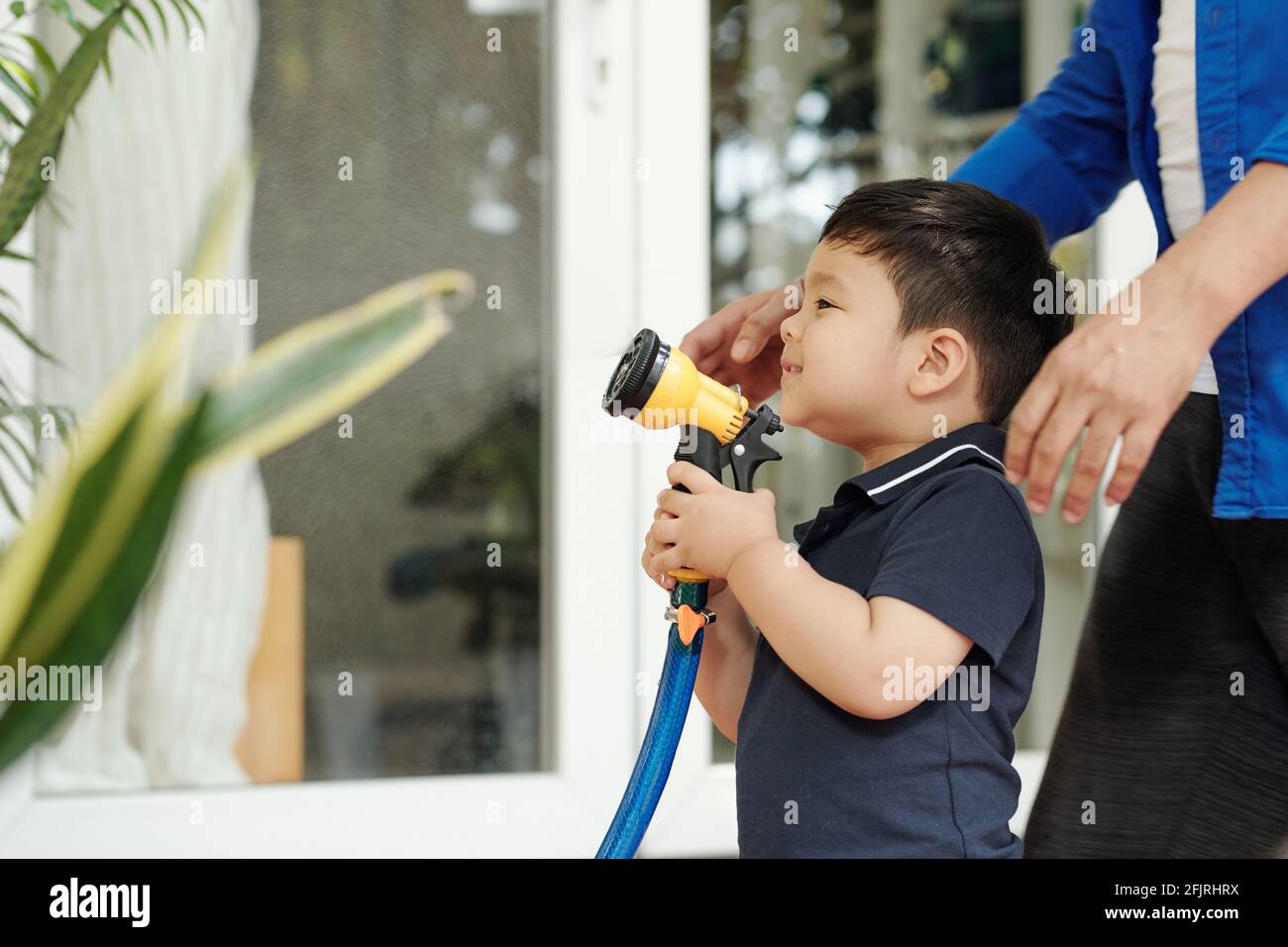 Excited happy little kid with hose nozzle enjoying watering plants in ...