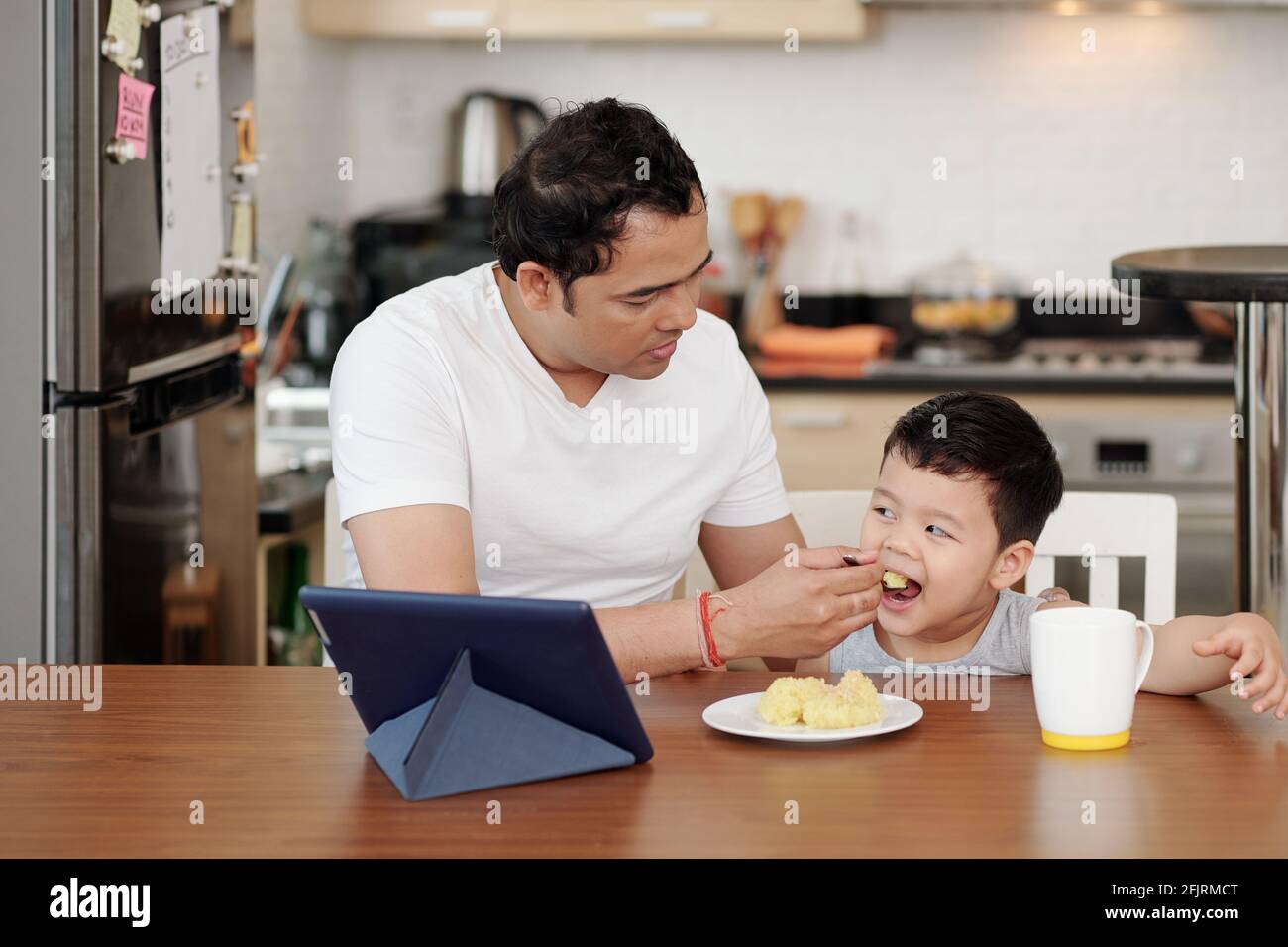 Father feeding his little son with mashed potato when they are watching ...