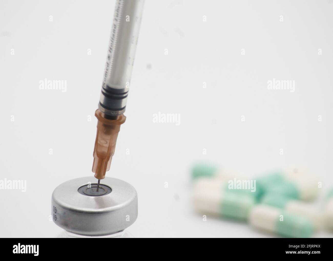 syringe stuck in vaccine vial on white background and pills out of ...