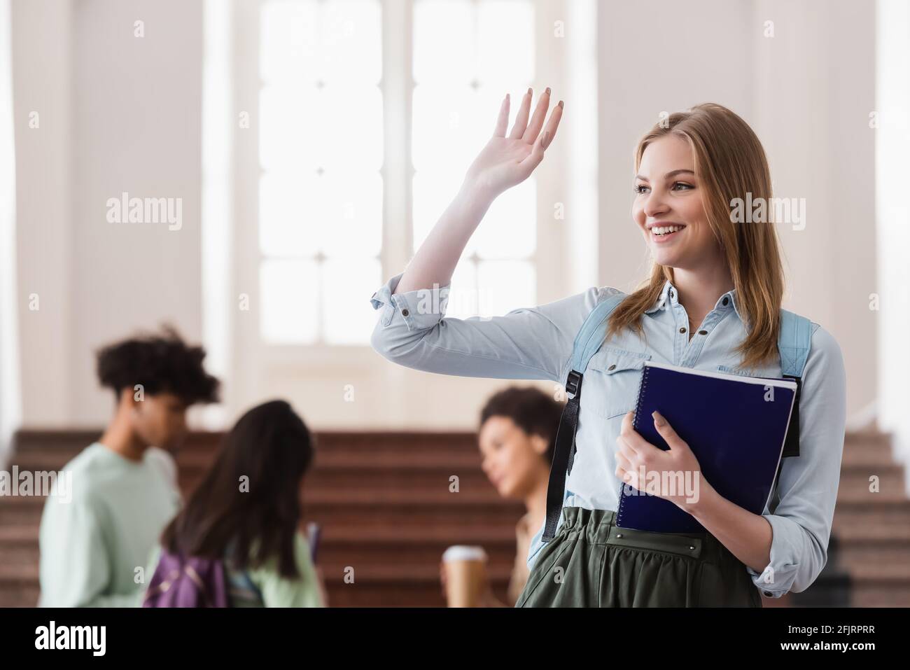 Happy student with notebook waving hand in hall of university Stock ...