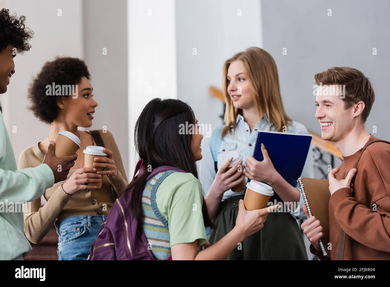 Positive multicultural students with paper cups talking in hall Stock ...