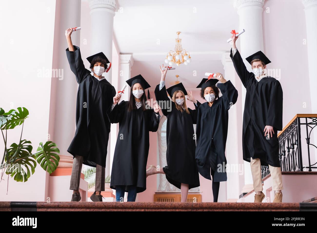 Multiethnic graduates in medical masks rising diplomas in university ...