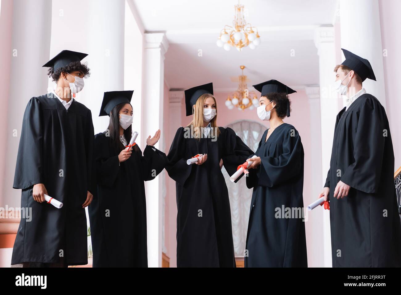 Multicultural graduates in protective masks holding diplomas and ...