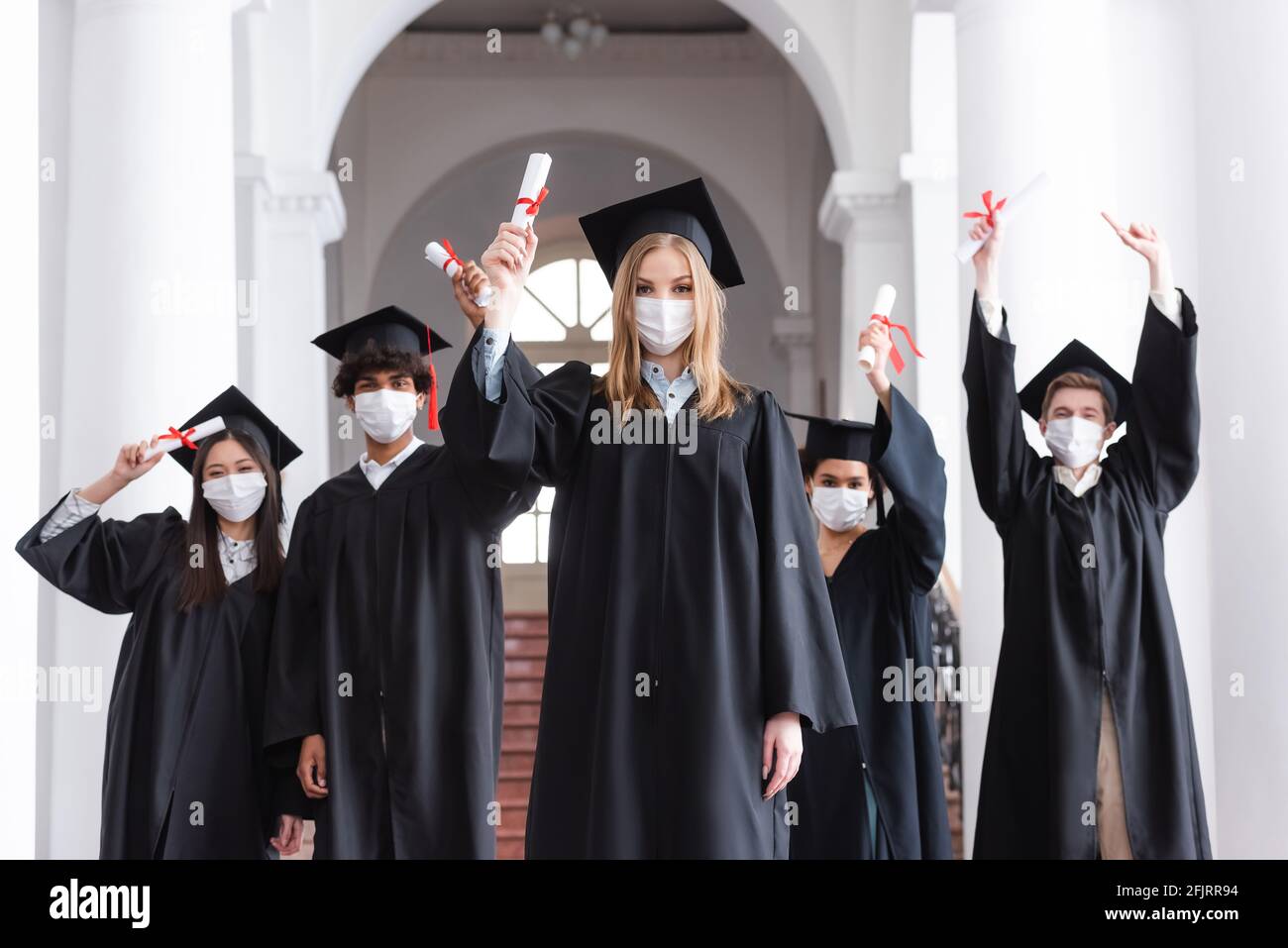 Multiethnic graduates in medical masks raising diplomas in university ...