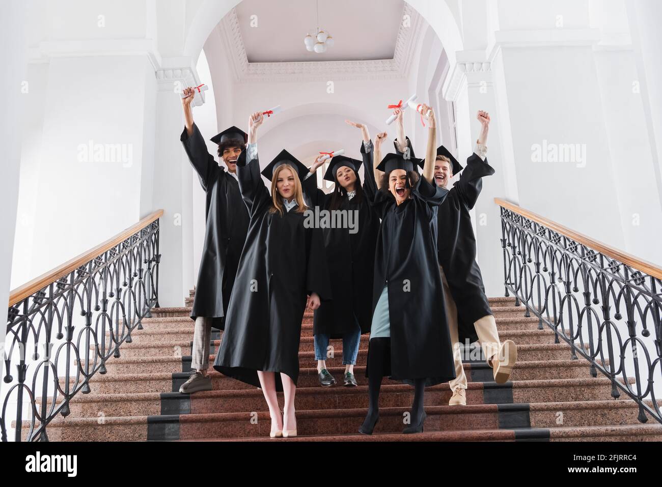 Excited multiethnic graduates with diplomas standing on stairs in ...