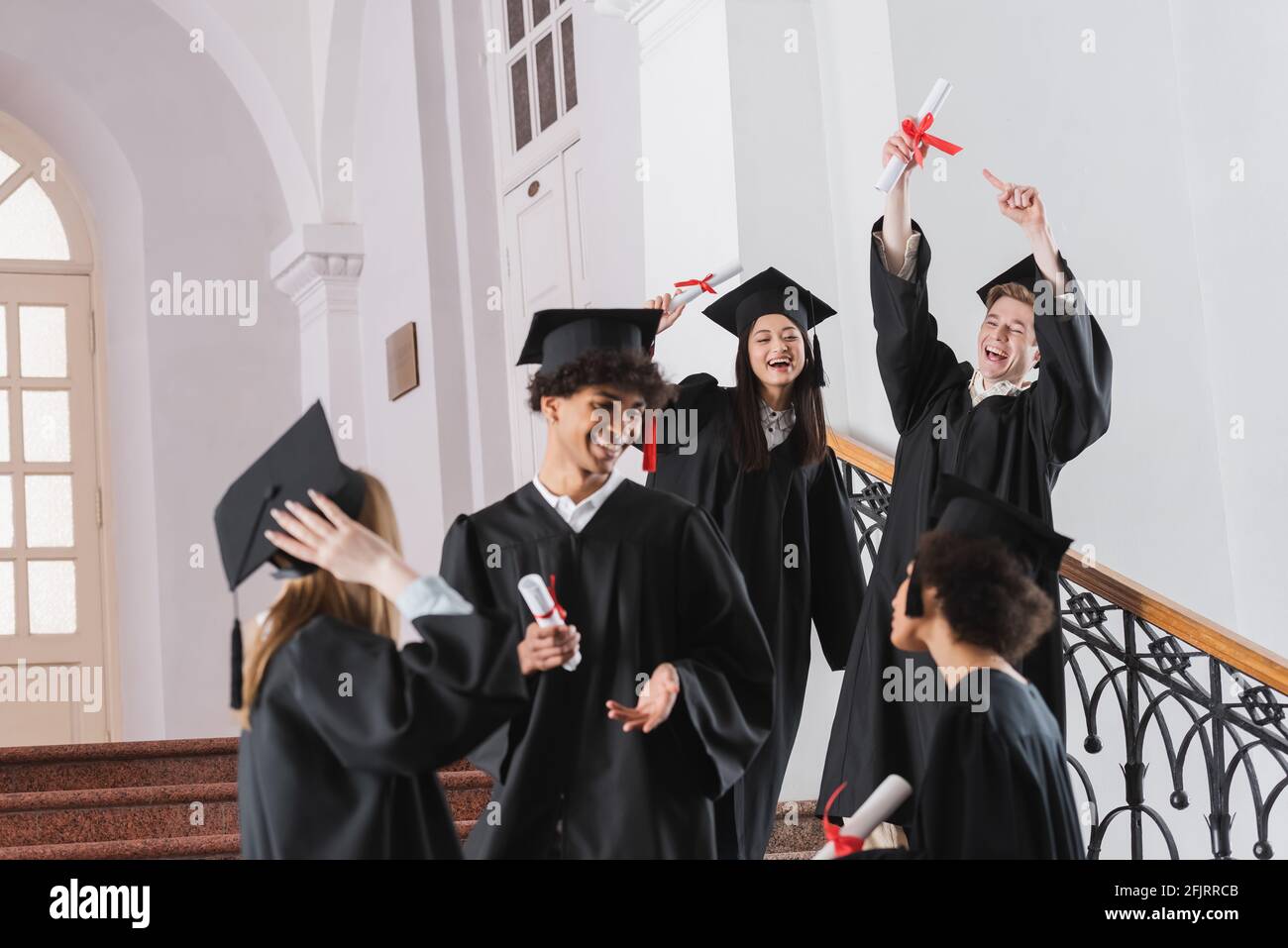 Excited graduate pointing at diploma near interracial friends Stock ...