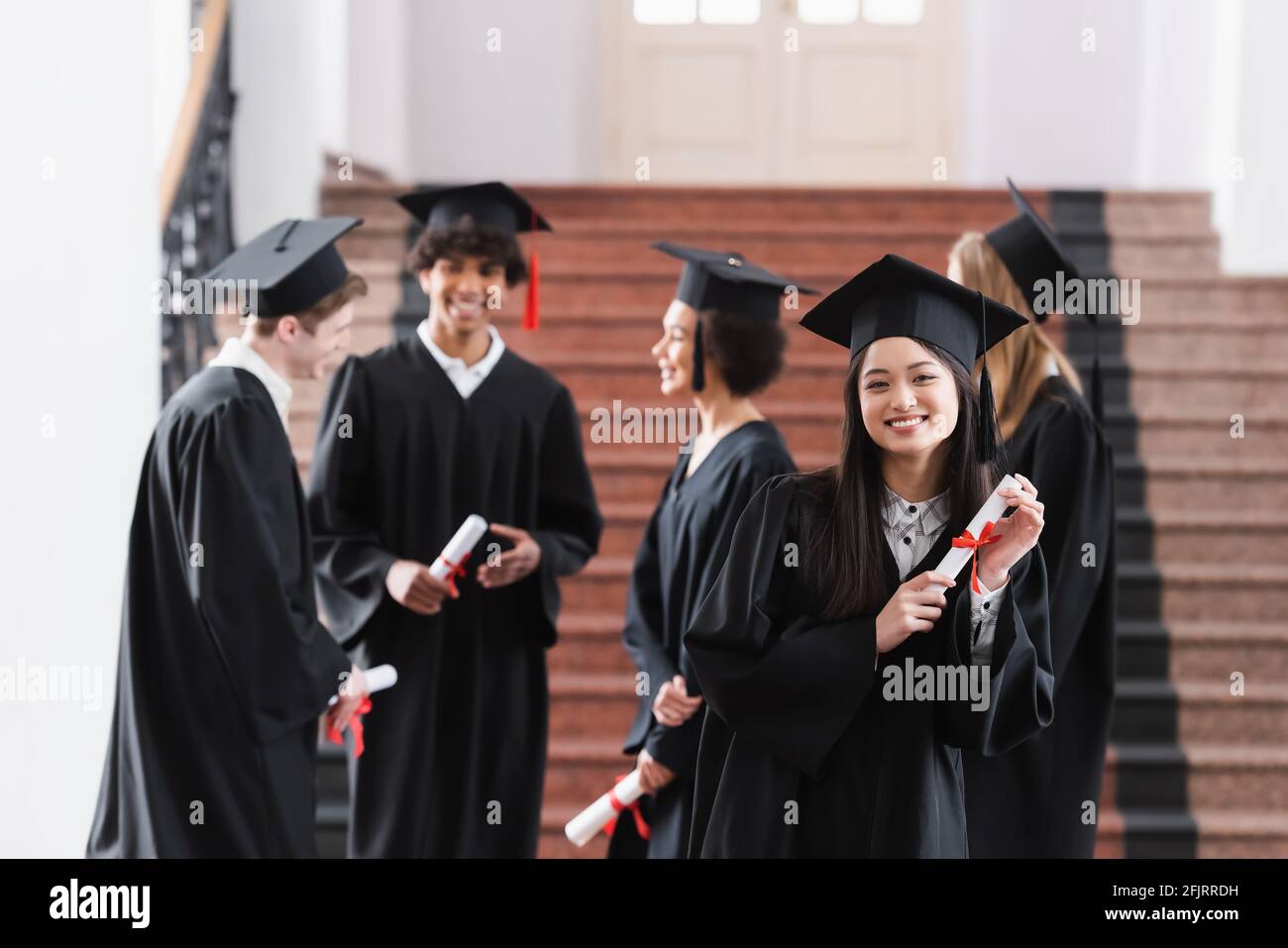 Happy asian graduate holding diploma near multiethnic friends Stock ...
