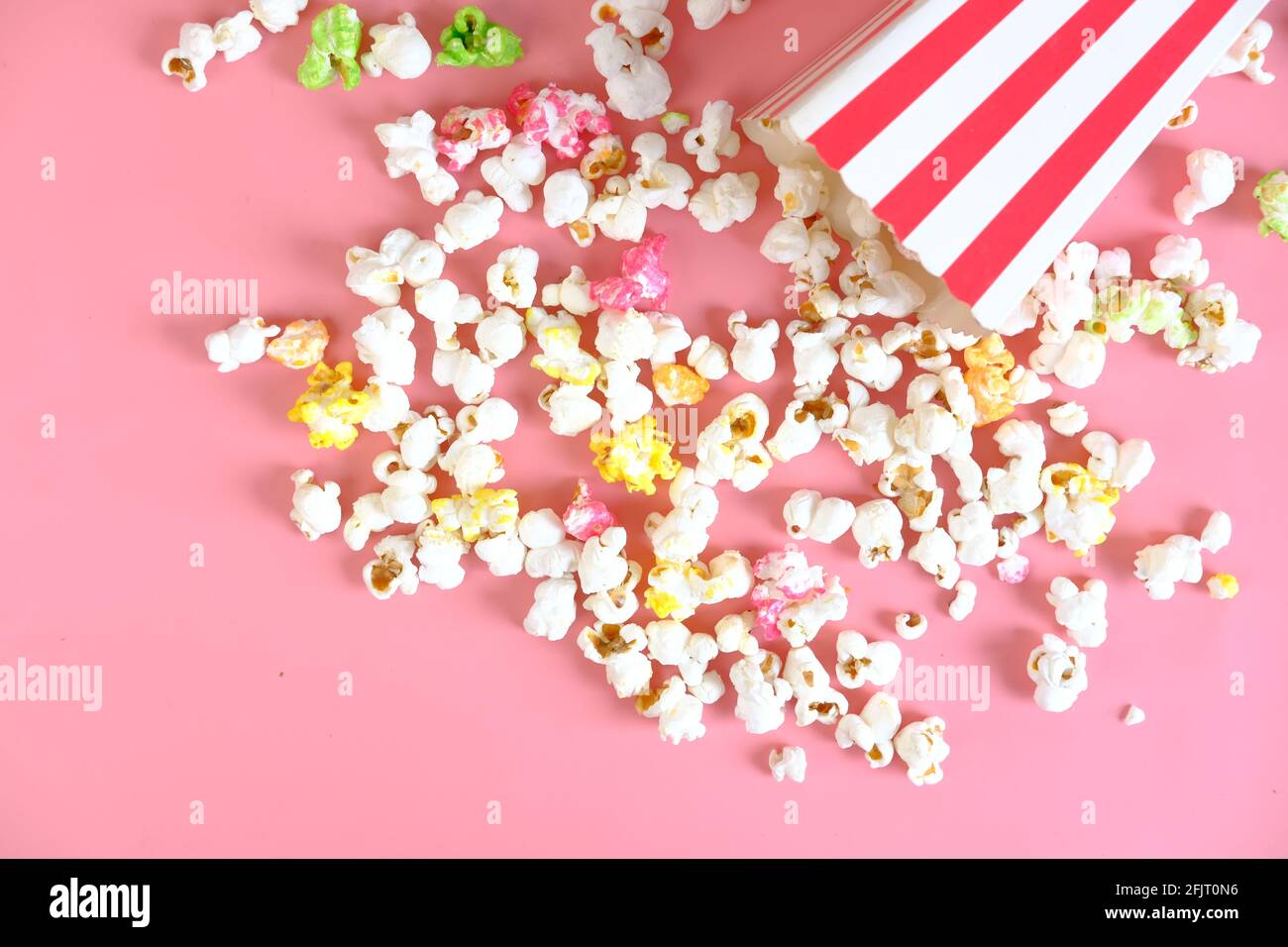 popcorn spilling from a container on pink background Stock Photo - Alamy