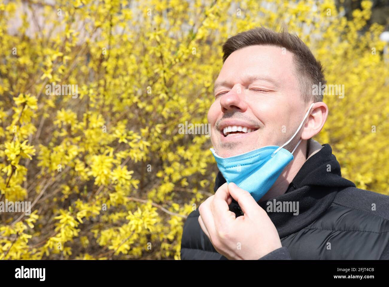 Young man taking off protective respirator from face near flowering ...