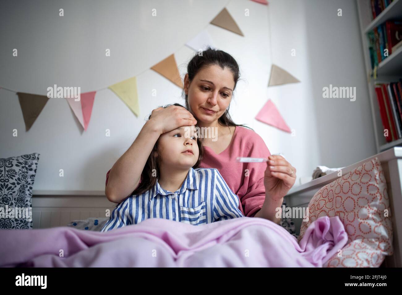 Mother looking after sick small daughter in bed at home, measuring ...