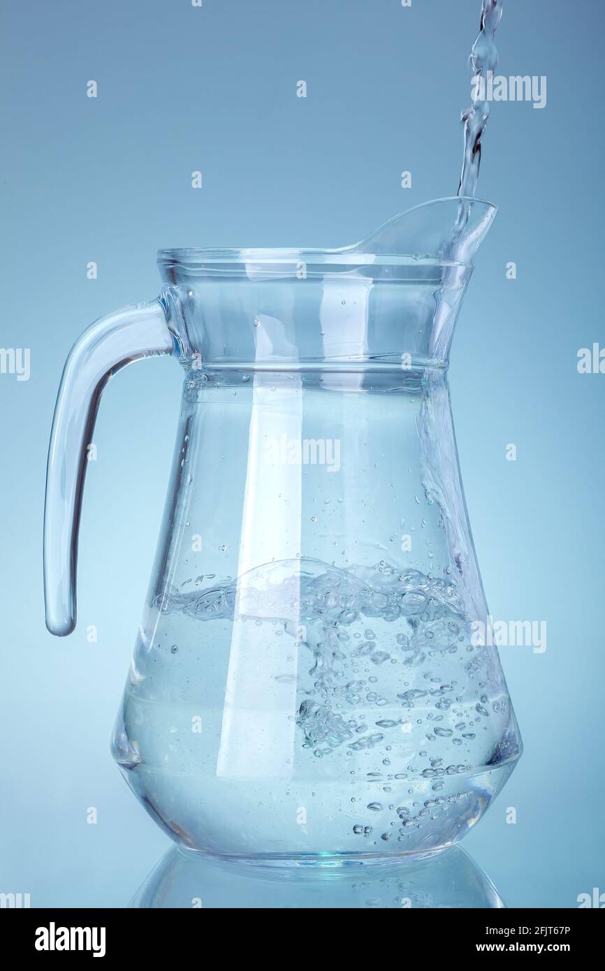 glass transparent jug for drinking water is filled with a stream of ...
