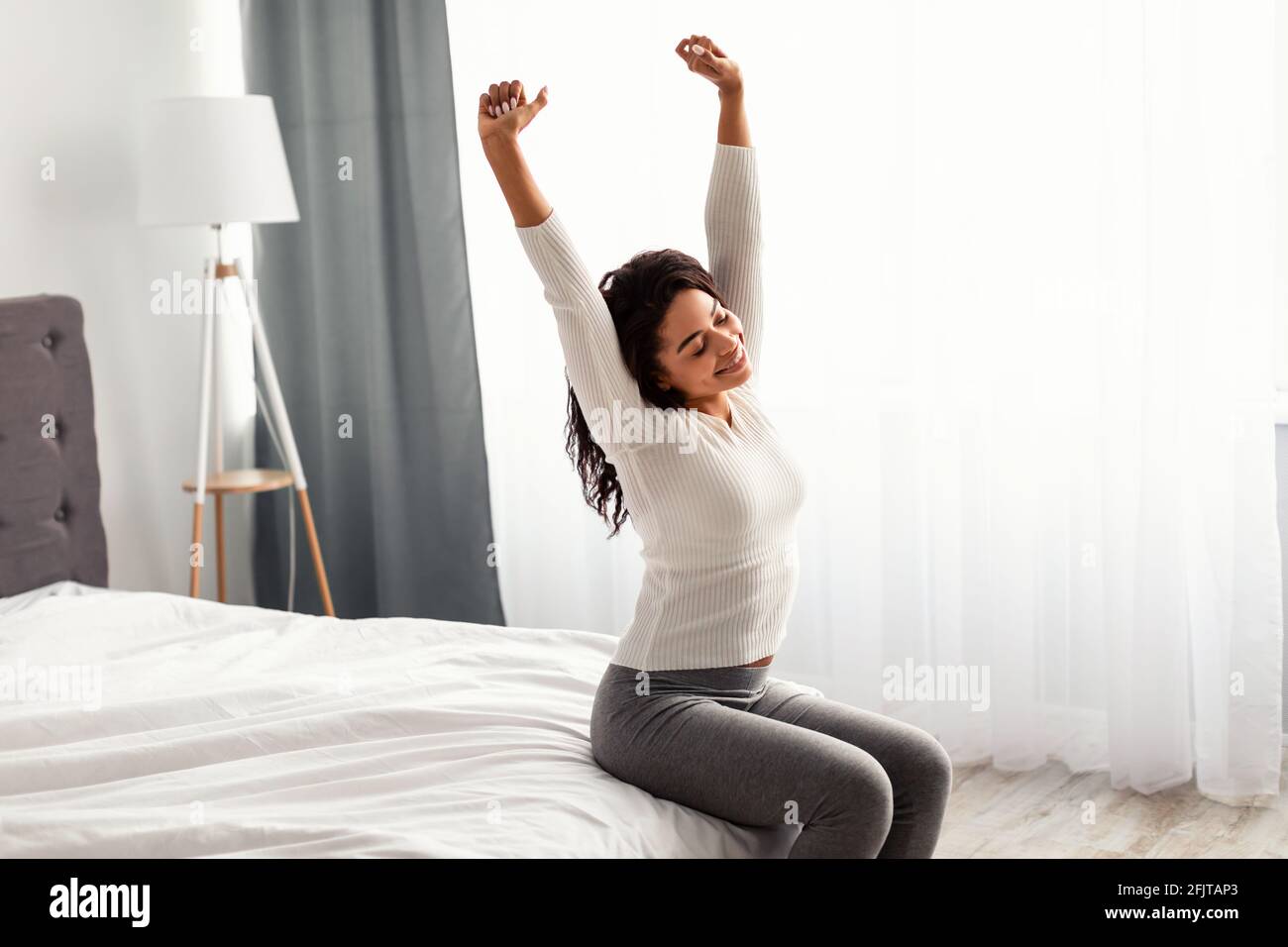 Peaceful black woman stretching arms and back sitting on bed Stock ...