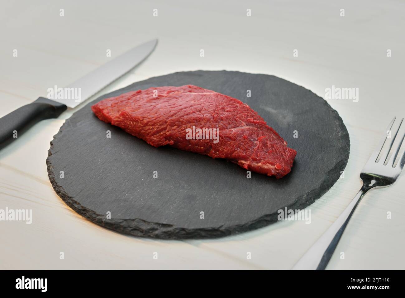 Edible raw meat. Fork and knife on wooden table Stock Photo - Alamy