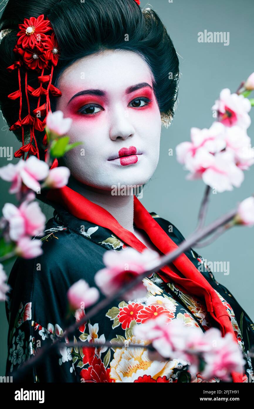 young pretty geisha in black kimono among sakura, asian ethno close up ...