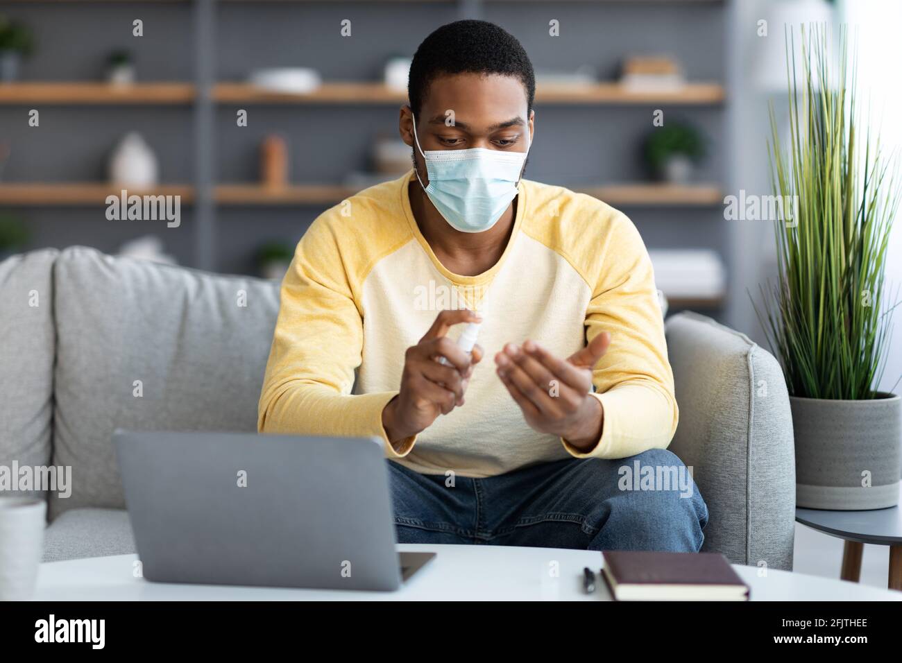 Black man freelancer in face mask cleaning hands with disinfector Stock ...