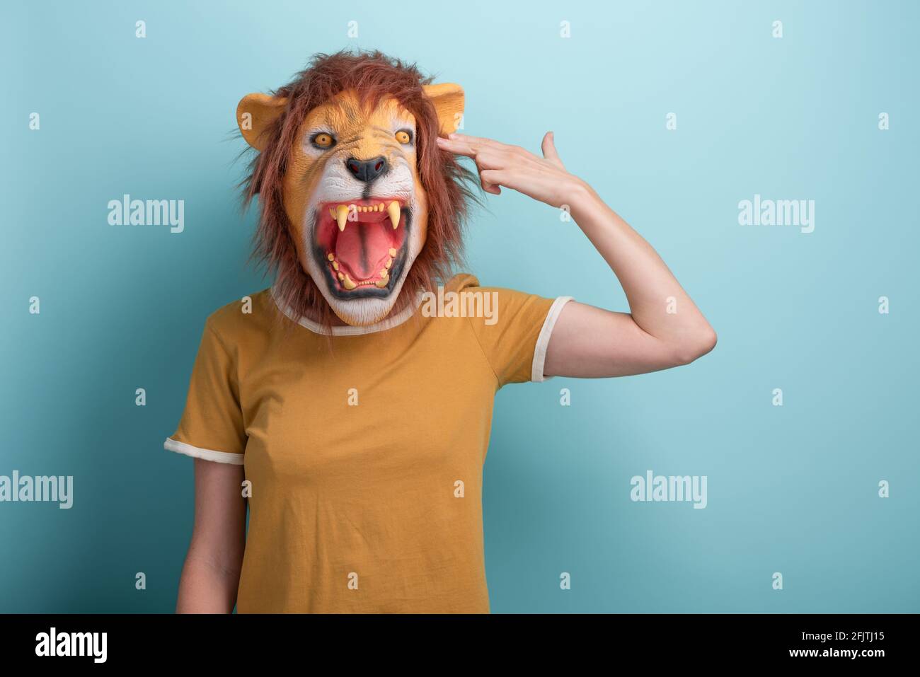 Young woman in lion mask pointing fingers to head in gun hand gesture ...
