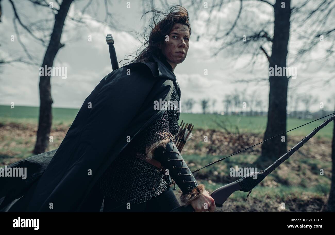 Woman in image of medieval warrior archer walks among forest with bow ...
