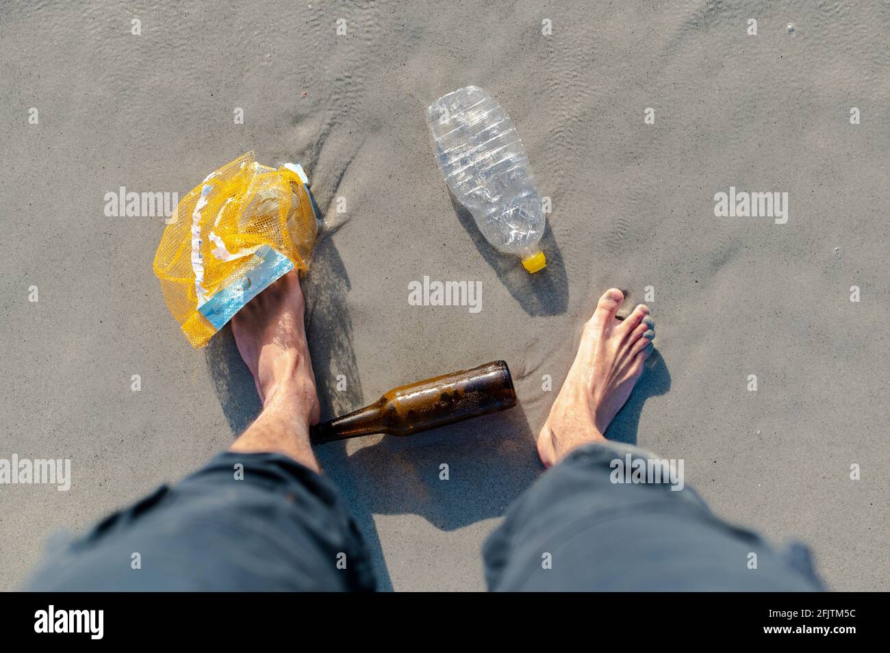 Top view man's feet on the beach surrounded by empty bottles, plastic ...