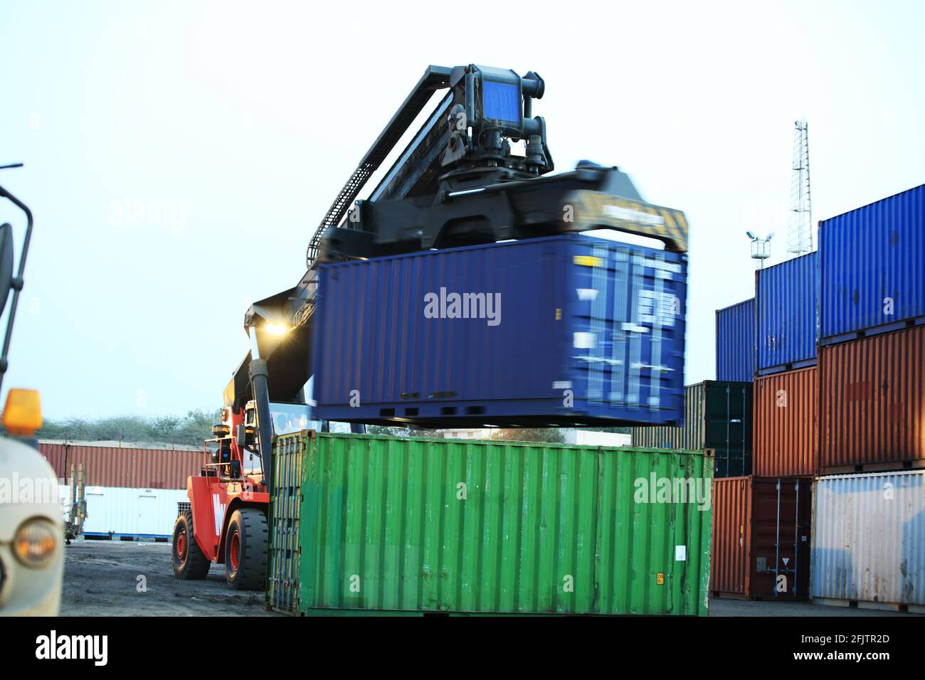 Forklift lifting and stacking cargo containers in a dockyard at evening ...