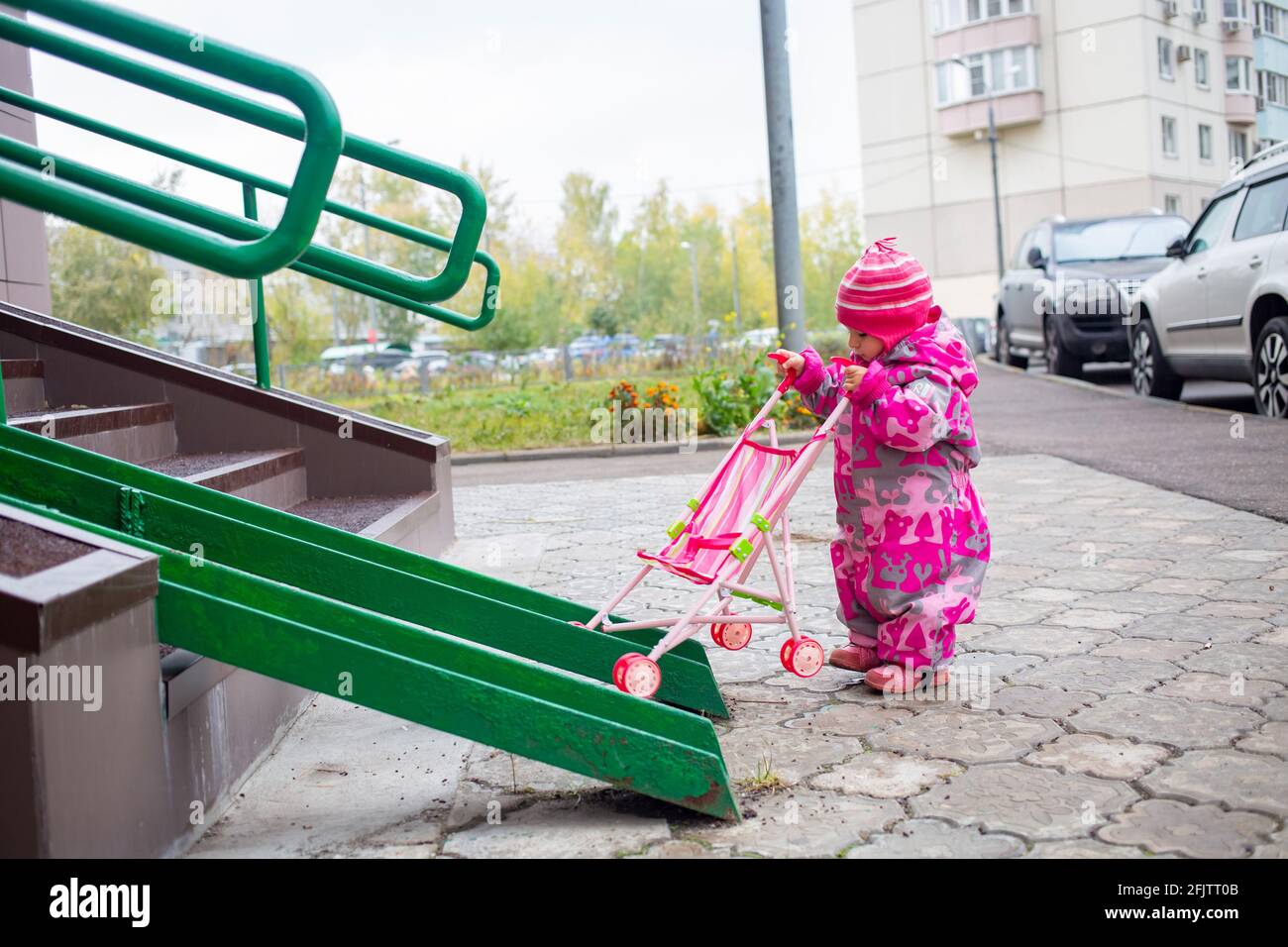 cute toddler with a toy stroller walks along steel railing ramp for ...