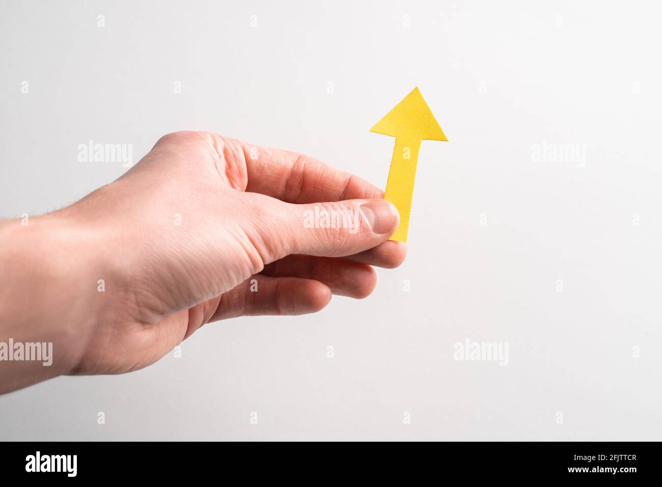 Hand holding a yellow paper arrow pointing up on white background Stock ...