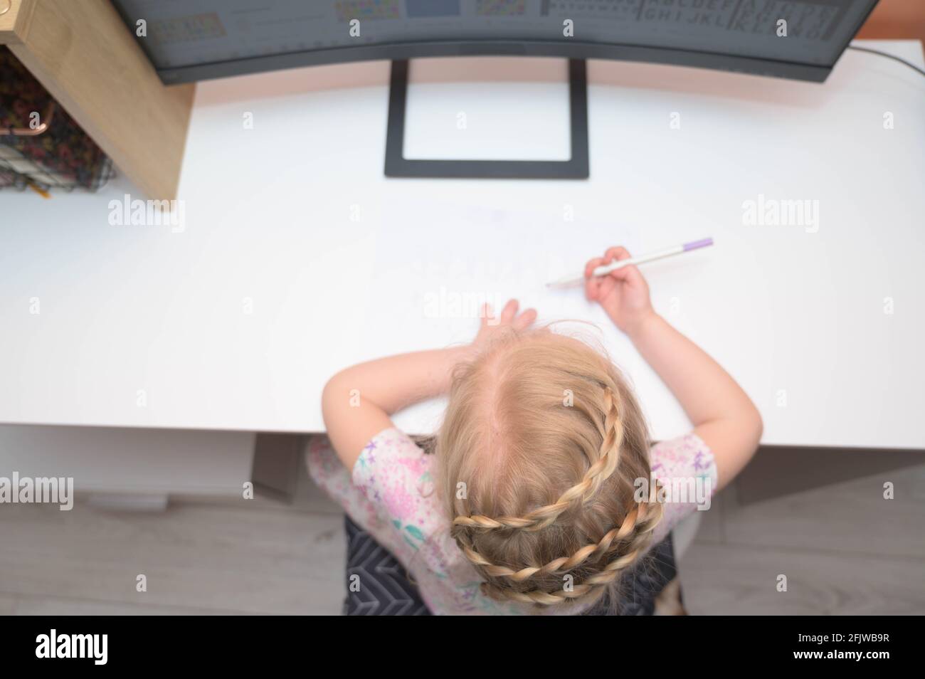Top view girl sitting at the desk, learning to write. Home schooling ...