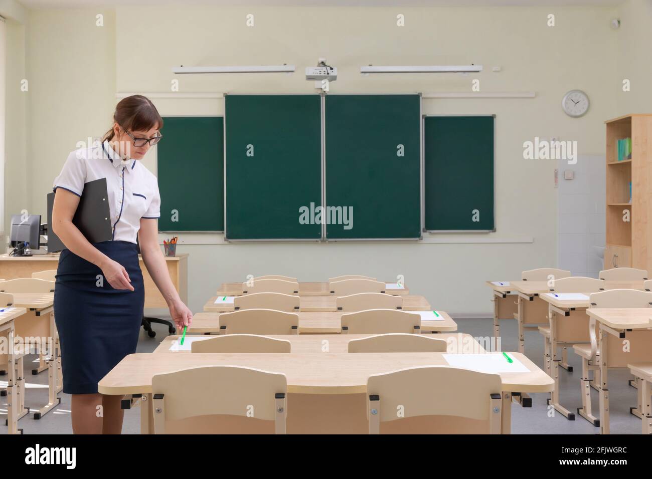 young pretty teacher woman in class at school lays out pens and sheets ...
