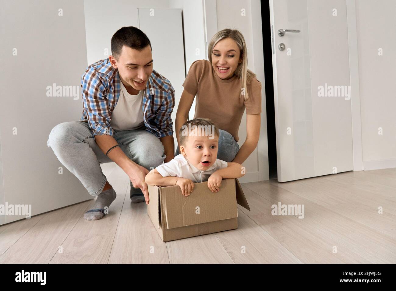 Funny excited child son riding in box on moving day with parents in new ...