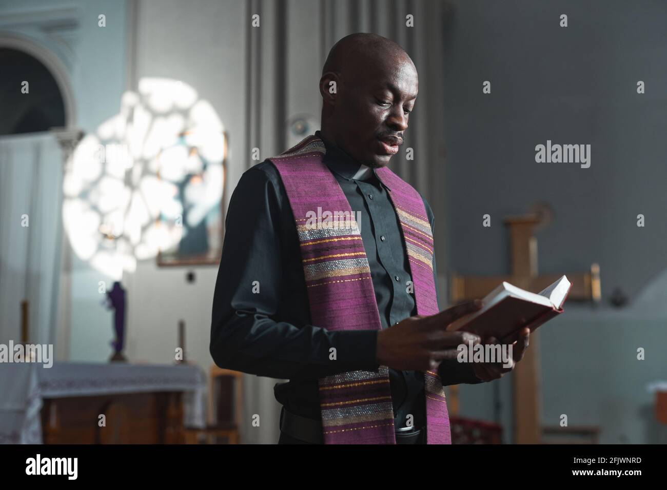 African young priest reading the Bible during mass while standing near ...