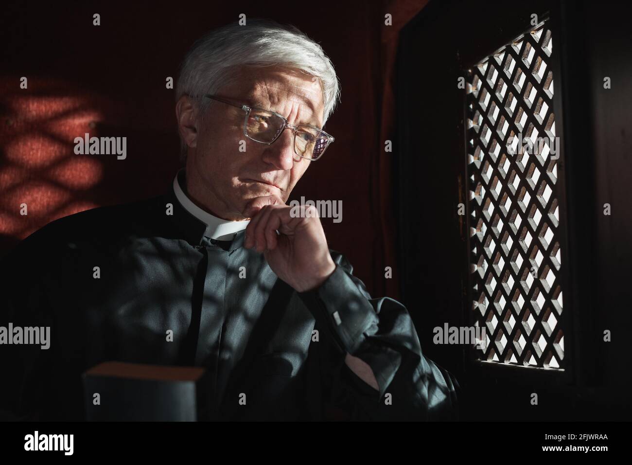 Senior priest sitting behind the grid and listening the confession in ...