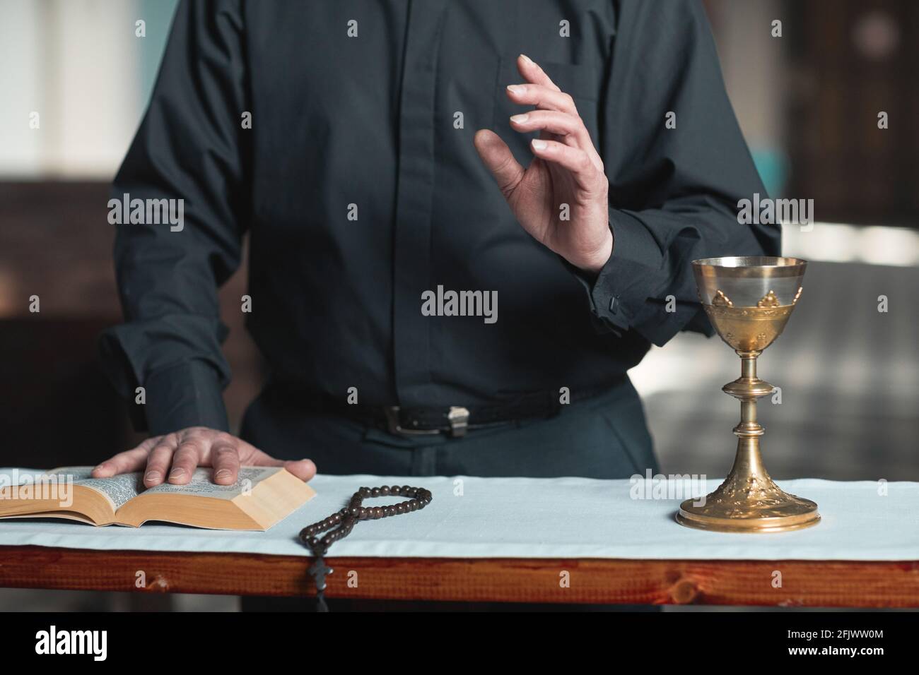 Close-up of priest standing at the altar with Bible and rosary beads ...