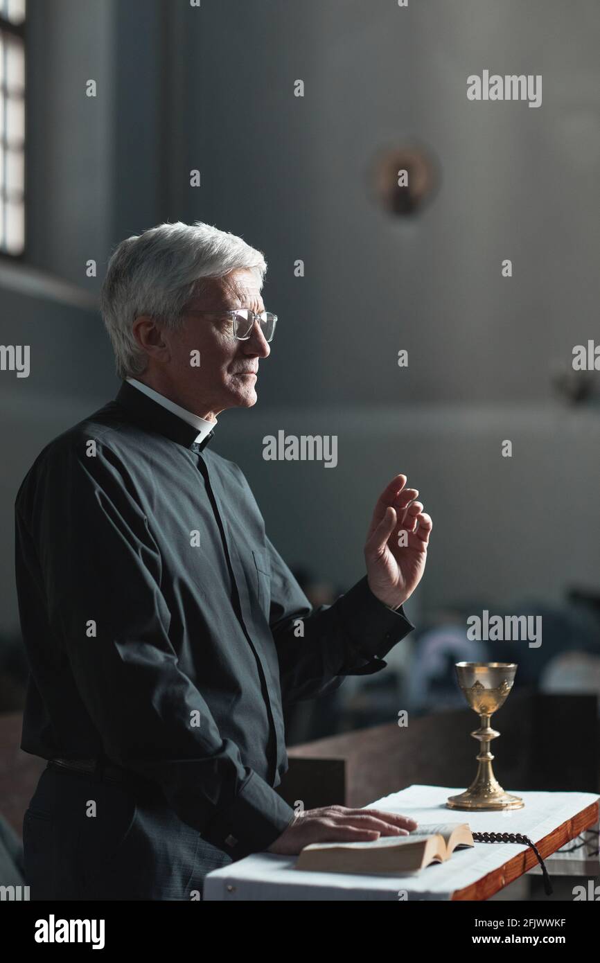 Senior man standing with the Bible in front of the altar and praying ...