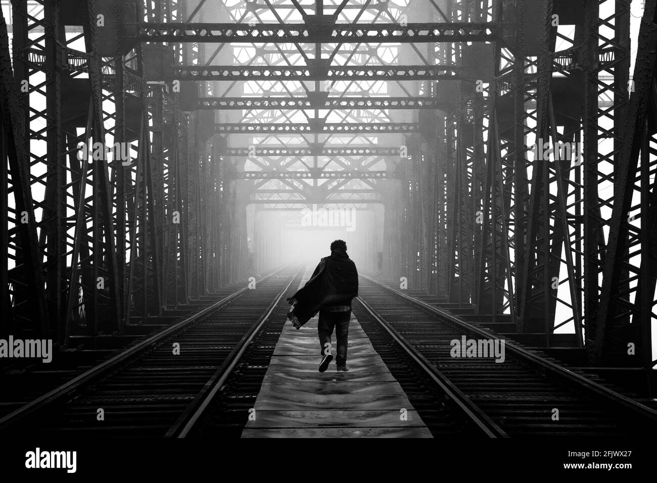 An alone walker walks through a rail-line in a very foggy winter ...