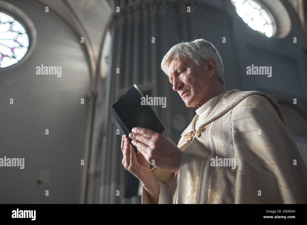 Senior priest in formal costume reading prayers while holding ceremony ...