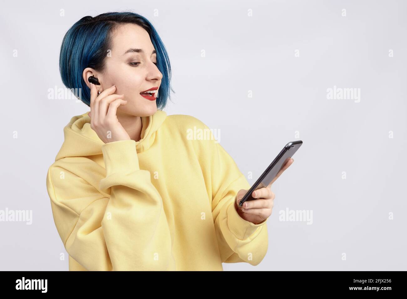 A female in yellow hoody holding wireless earphones. The white ...