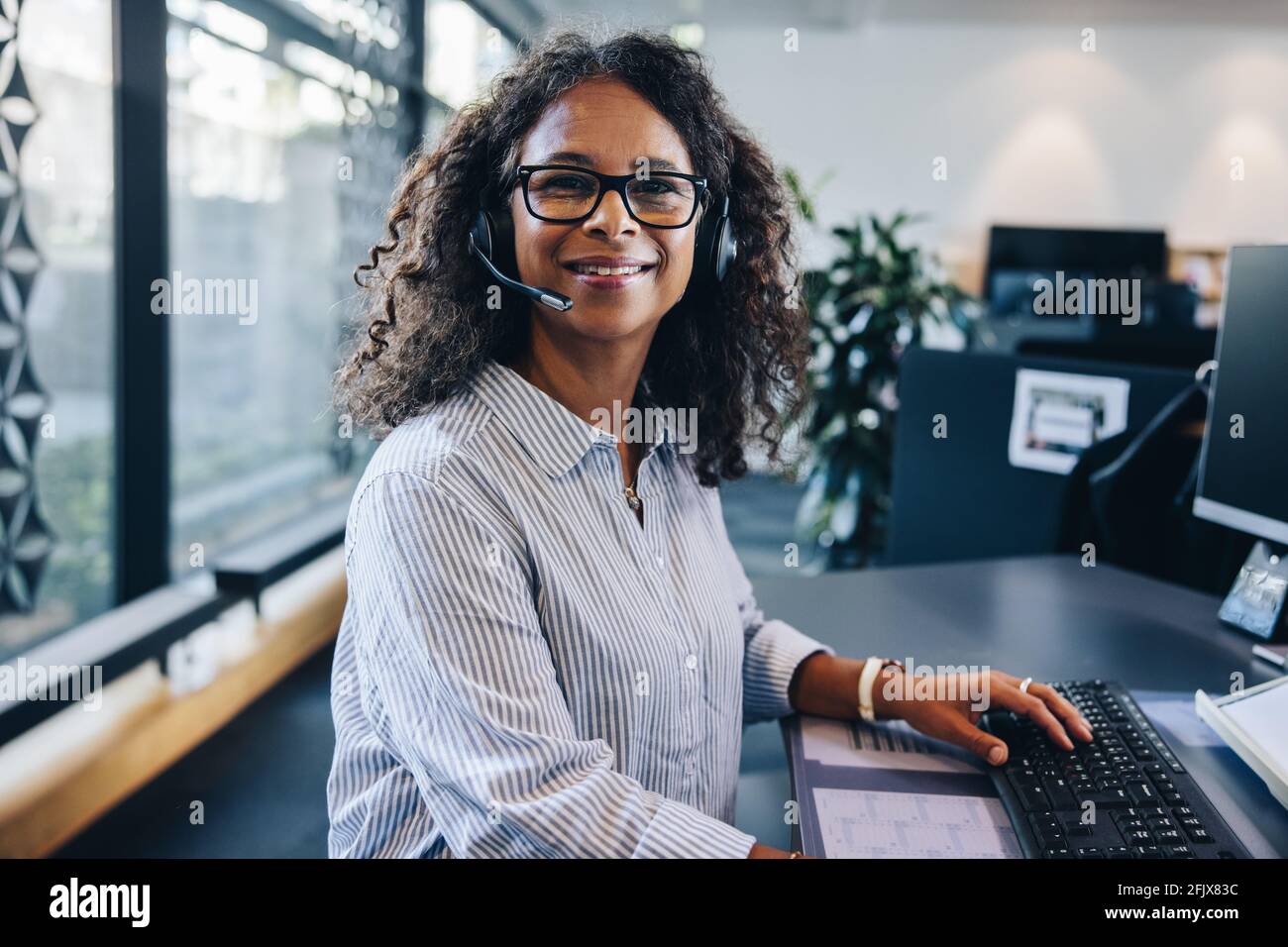 Portrait of a confident female executive wearing headset sitting in ...