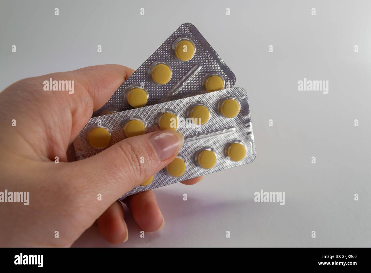 Two blisters with yellow pills in a female hand on a light background ...