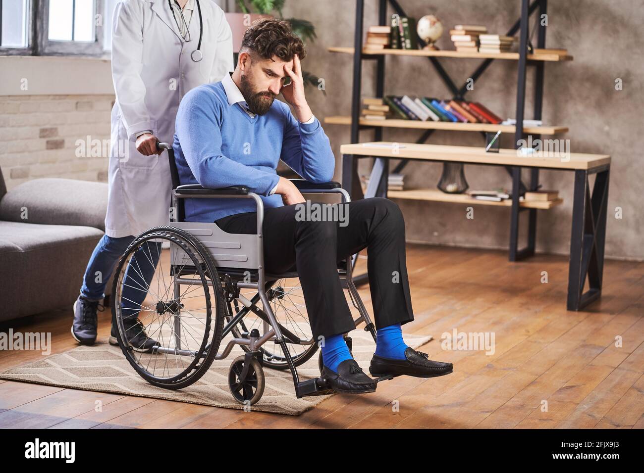 Doctor pushing a wheelchair with a sad disabled man Stock Photo - Alamy