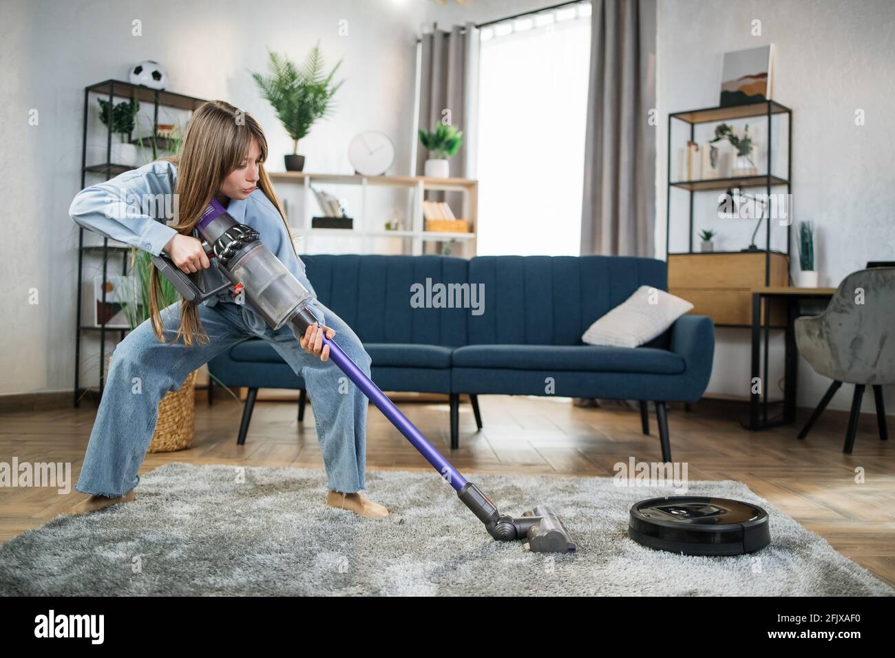 Happy pretty lady doing chores using two wireless vacuum cleaners ...