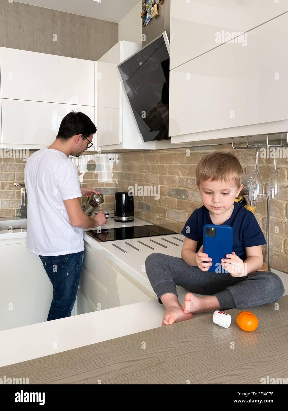 Boy using telephone while his father making tea Stock Photo - Alamy